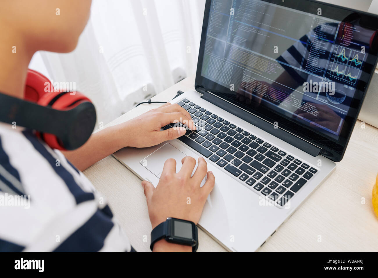 Teenage boy with smartwatch and heaphones programming on laptop, he is ...