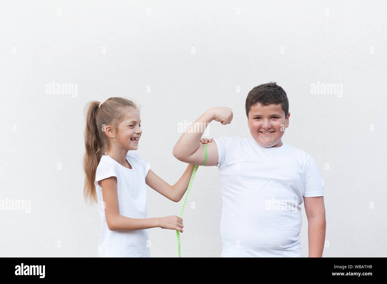 happy laughing small slim girl measuring thick smiling kid muscle with ...