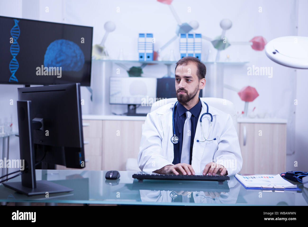Young handsome doctor working and typing in his cabinet. Doctor using ...