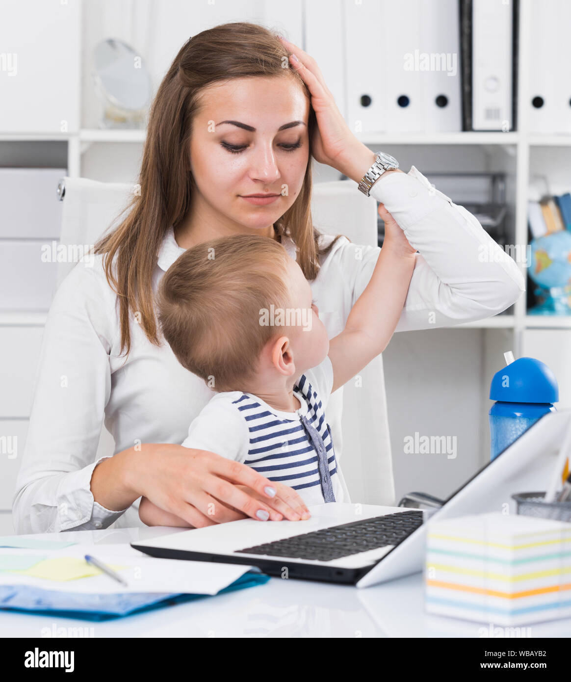 Perplexed girl with child is having issue while working behind laptop ...