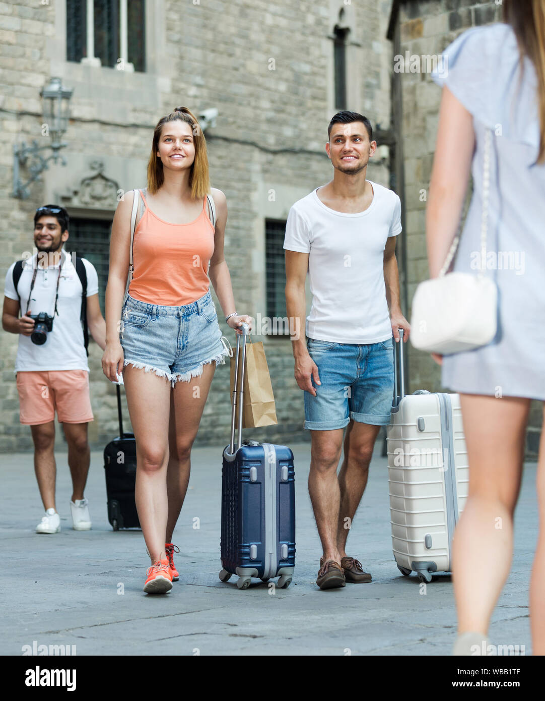 Portrait of smiling couple tourists taking walk and dragging luggage ...