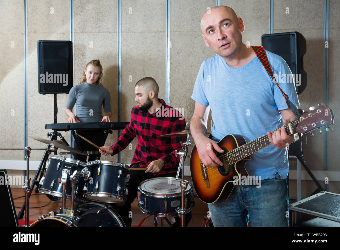 Emotional male singer with guitar rehearsing with band of drummer and ...