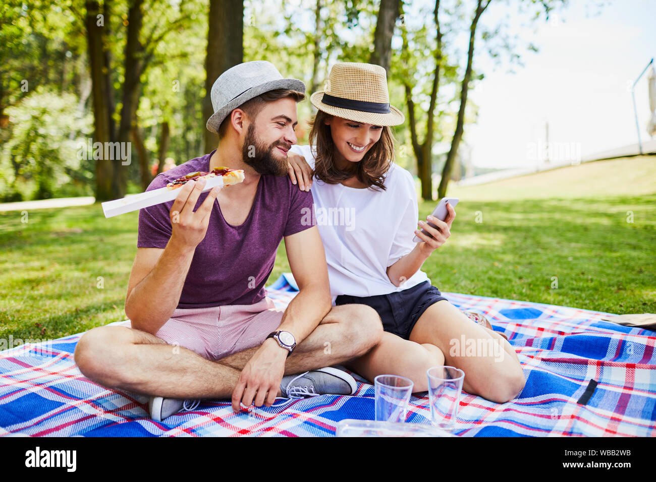 Young couple on picnic eating and looking at phone while sitting ...