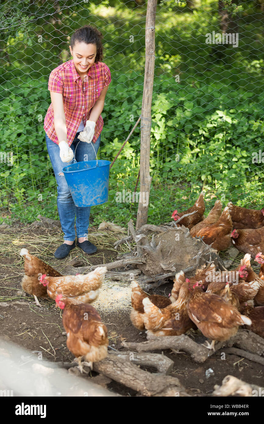 cheerful smiling female farmer standing with bucket and feeding ...