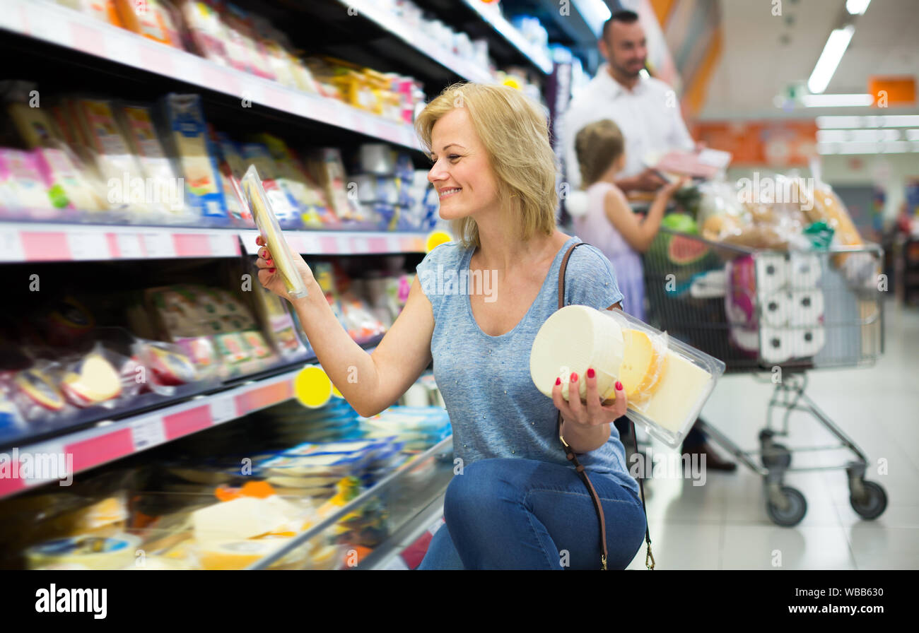 Female customer selecting cheese in refrigerated section in hypermarket ...