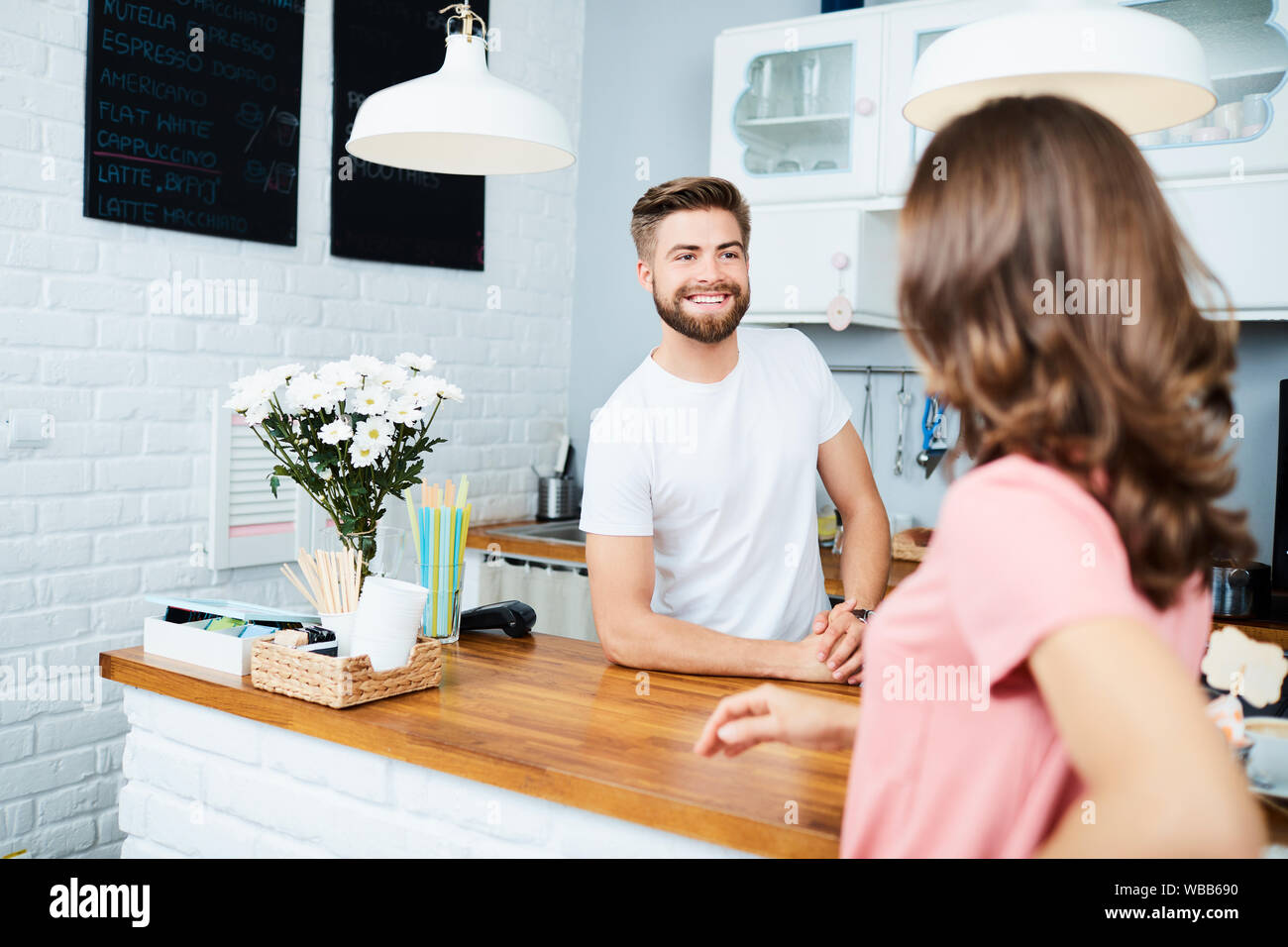 Cheerful bartender standing behind counter and taking order from female ...