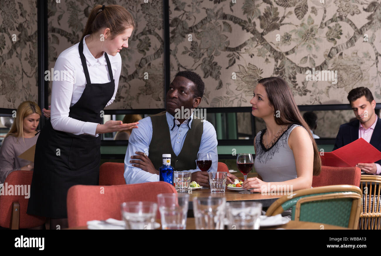 Happy young couple kindly talking with polite waitress in cozy ...