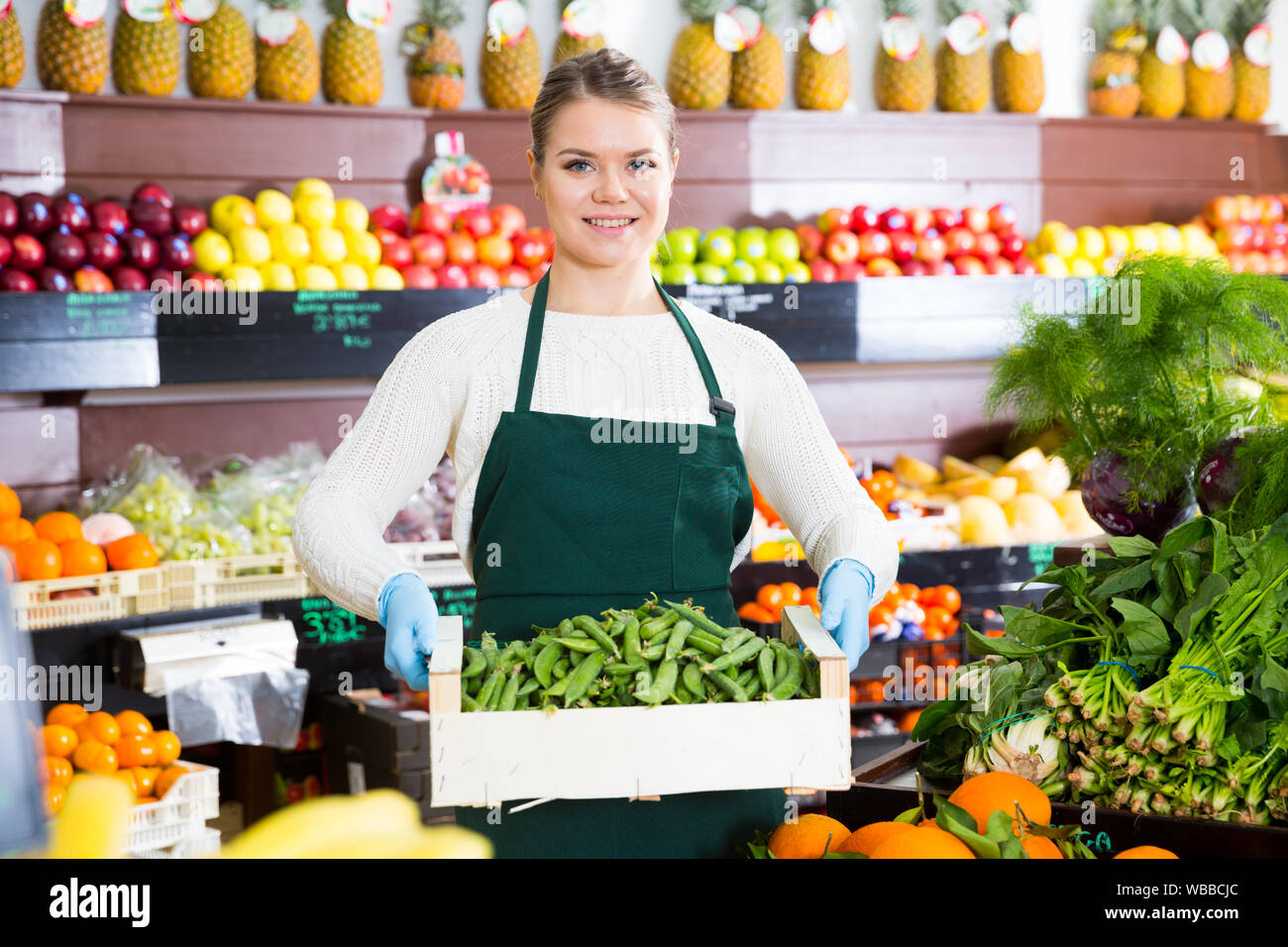 Friendly young woman worker posing with box of green beans at ...