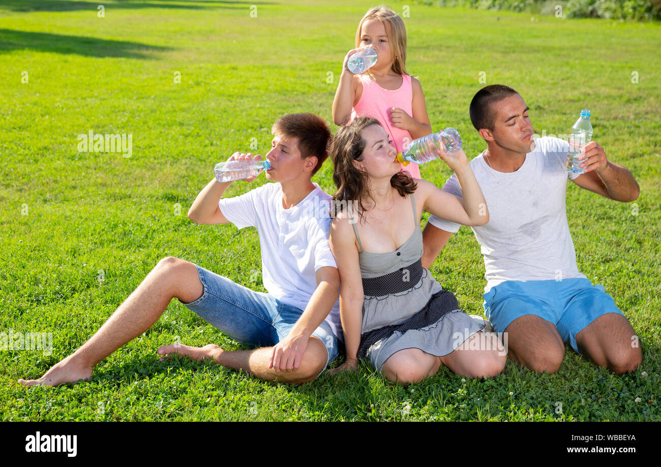 Parents with teenager son and daughter drinking cold water from plastic ...
