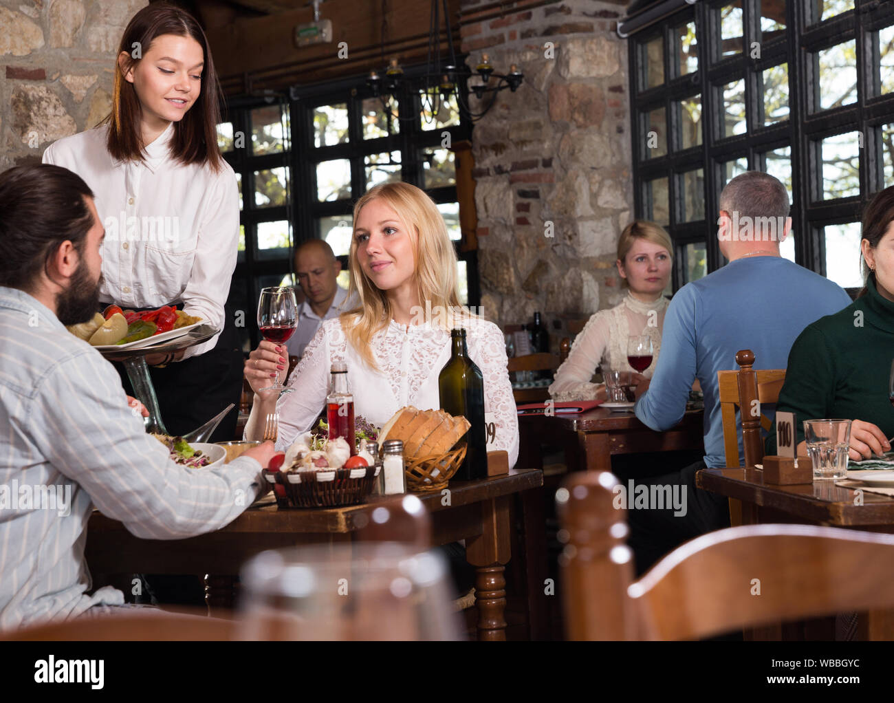 Polite waitress bringing ordered dishes to guests in comfortable ...