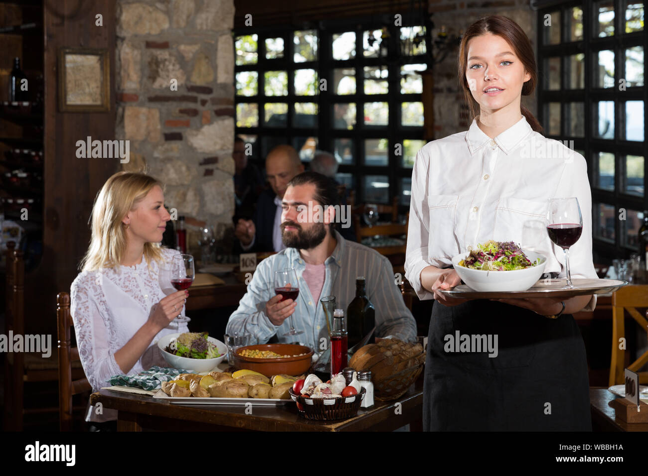 Positive woman waiter demonstrating country restaurant to visitors ...