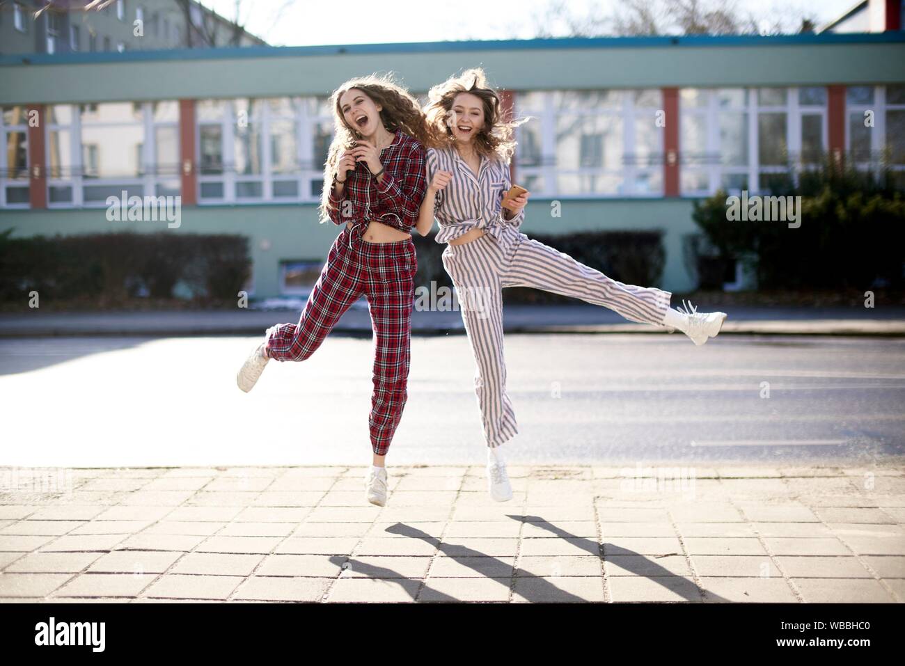 two exuberant women jumping against each other, wearing pyjamas at ...