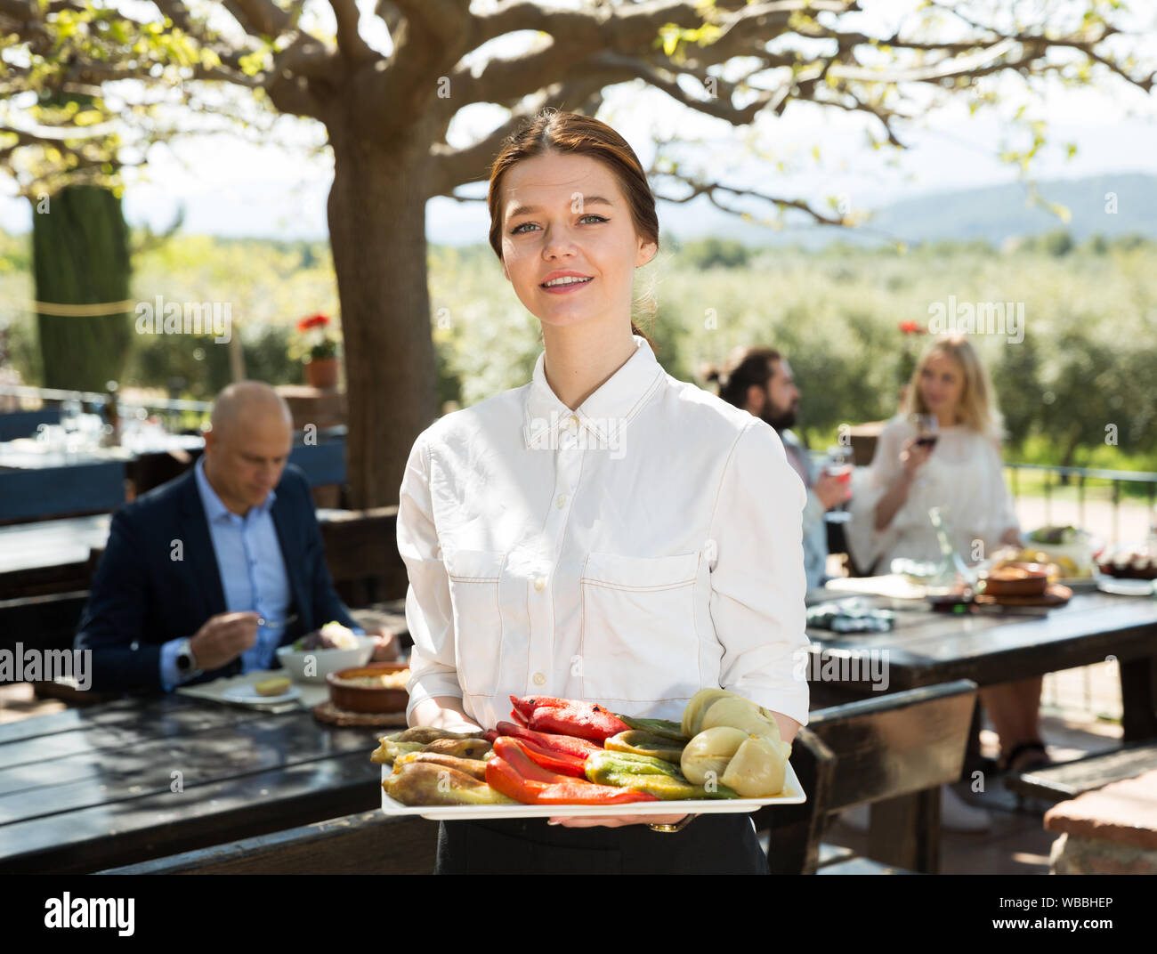 Positive woman waiter demonstrating open-air restaurant to visitors ...