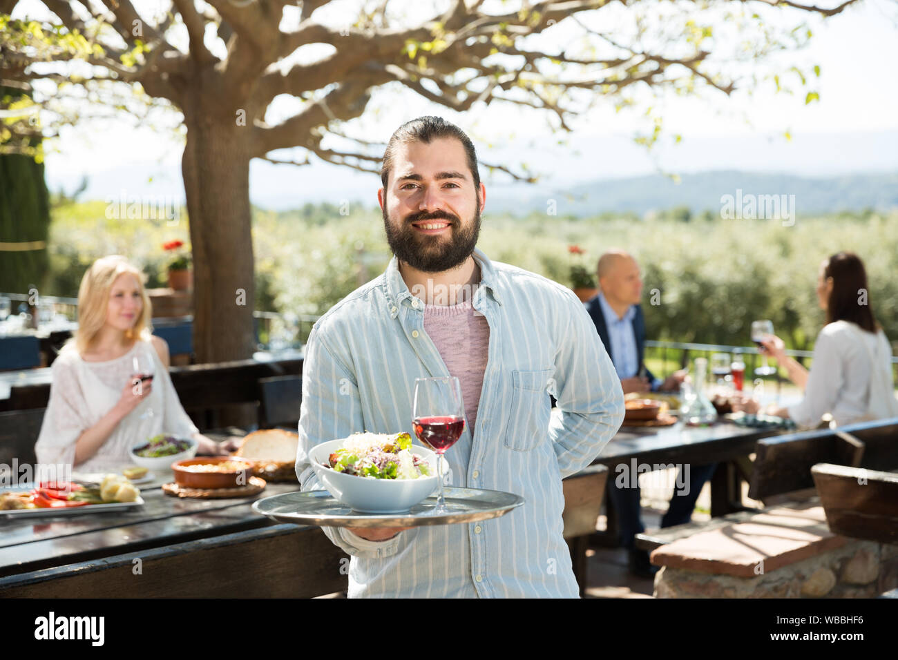 Adult beard waiter who is standing with order at country outdoor ...