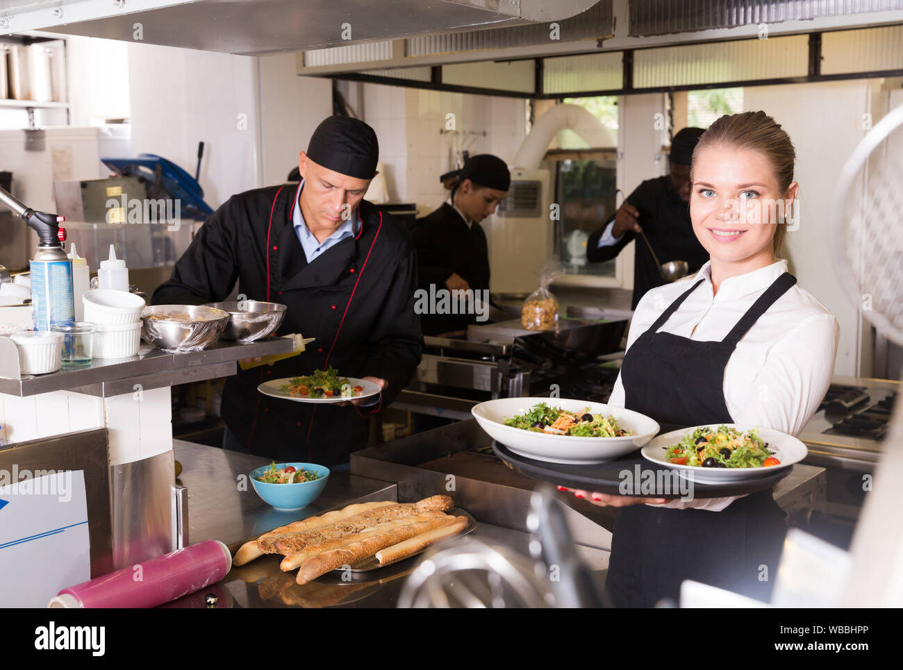Successful young waitress standing in restaurant kitchen with ordered ...