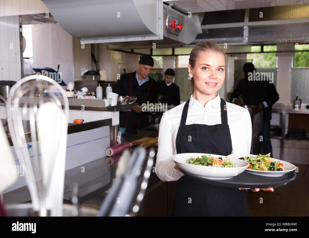 Successful young waitress standing in restaurant kitchen with ordered ...