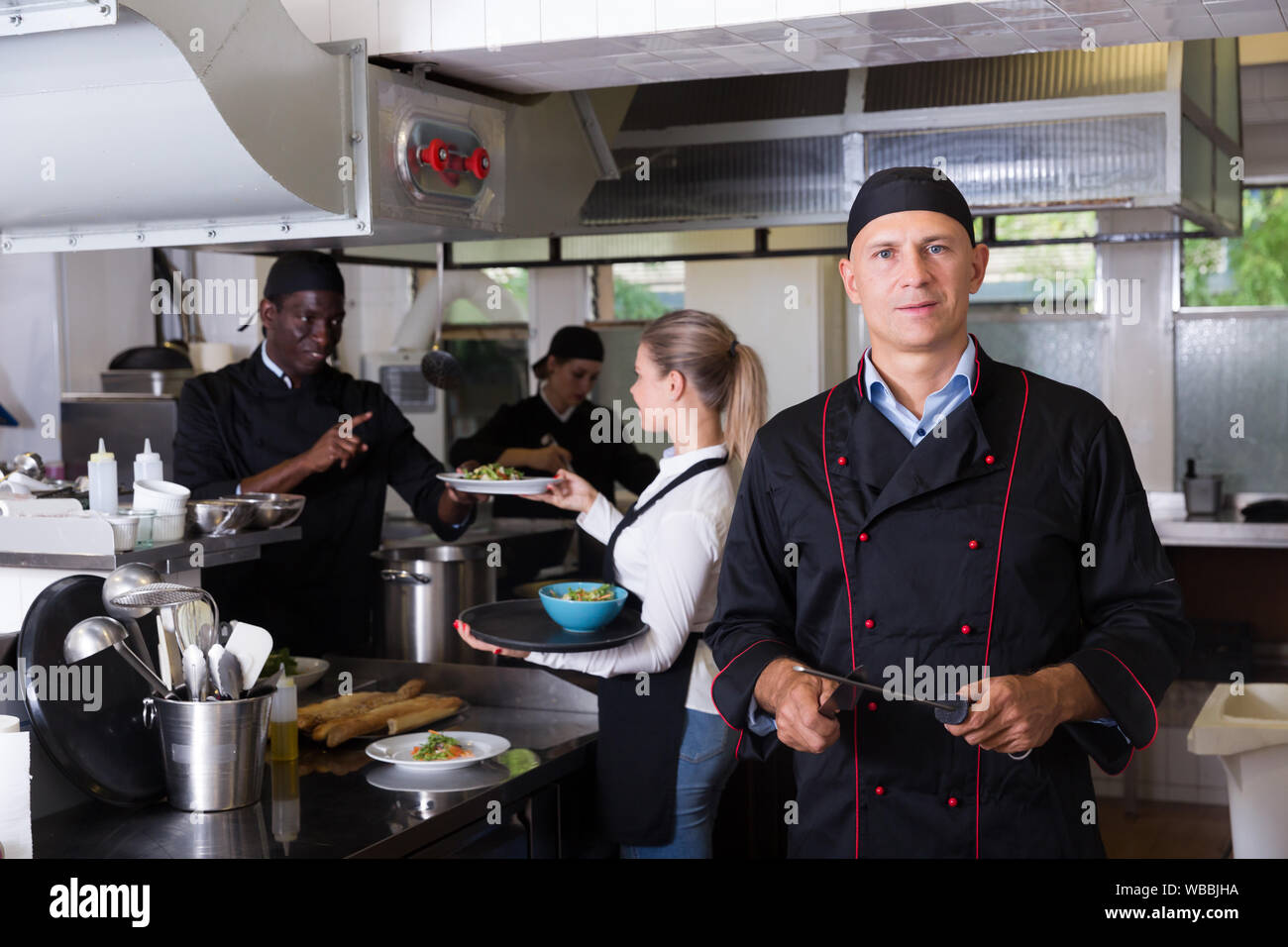 Portrait of confident male chef in restaurant kitchen with busy ...