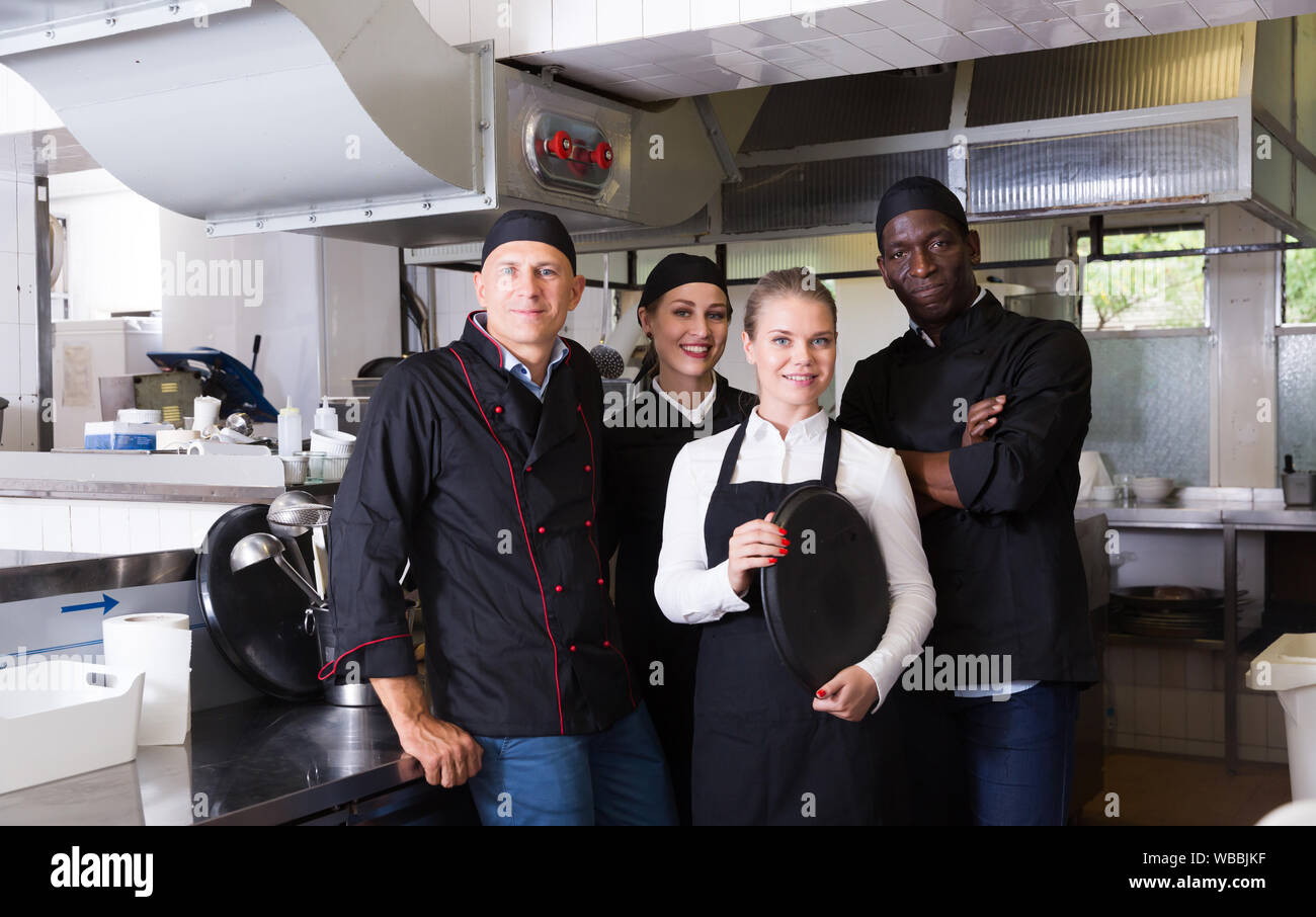 Portrait of confident smiling team of chefs in interior of restaurant ...