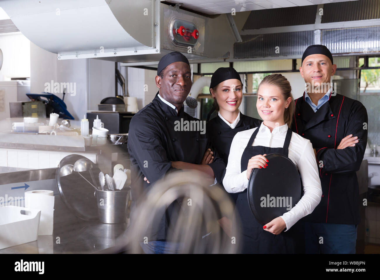 Portrait of confident smiling team of chefs in interior of restaurant ...