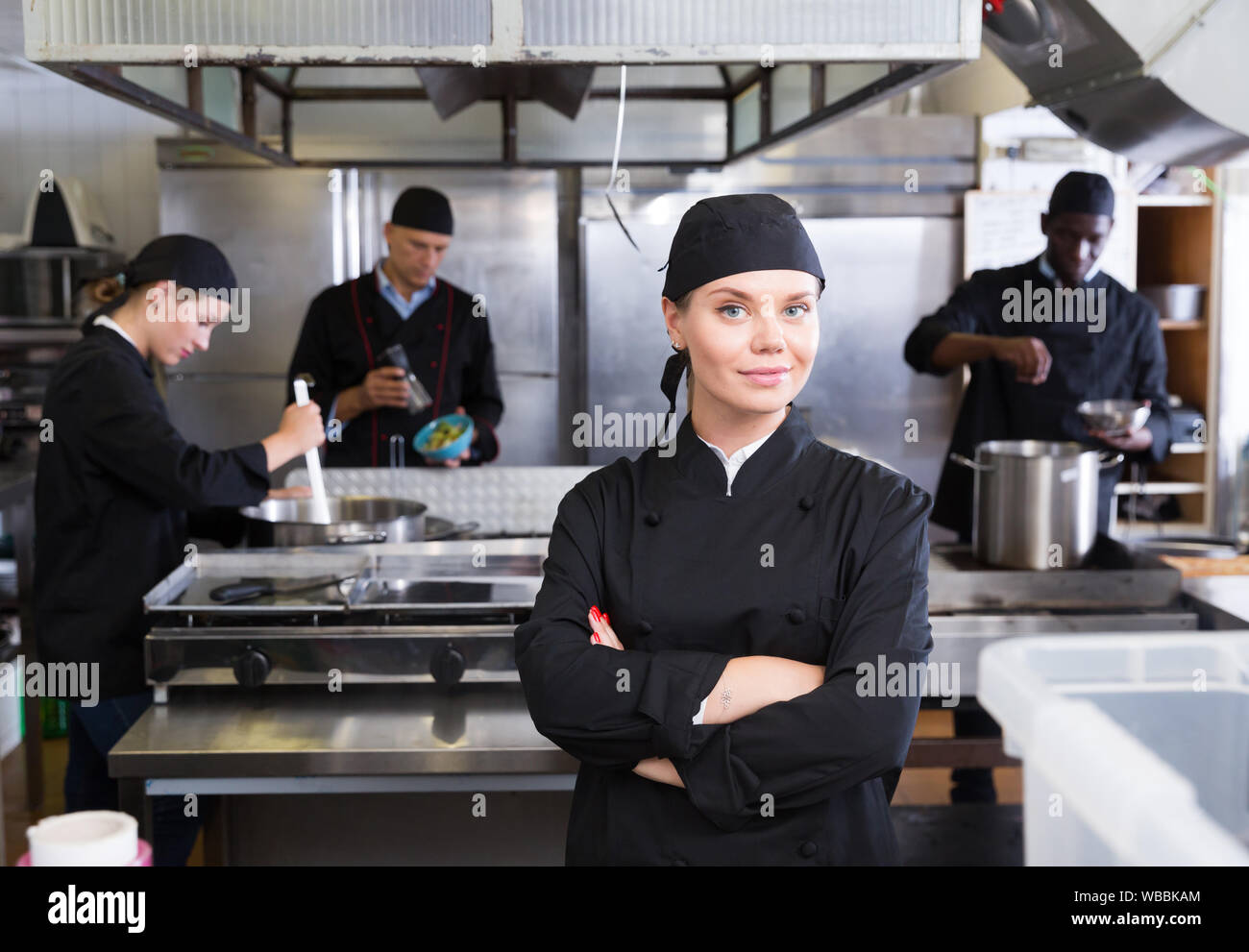 Attractive female chef of restaurant standing in professional kitchen ...