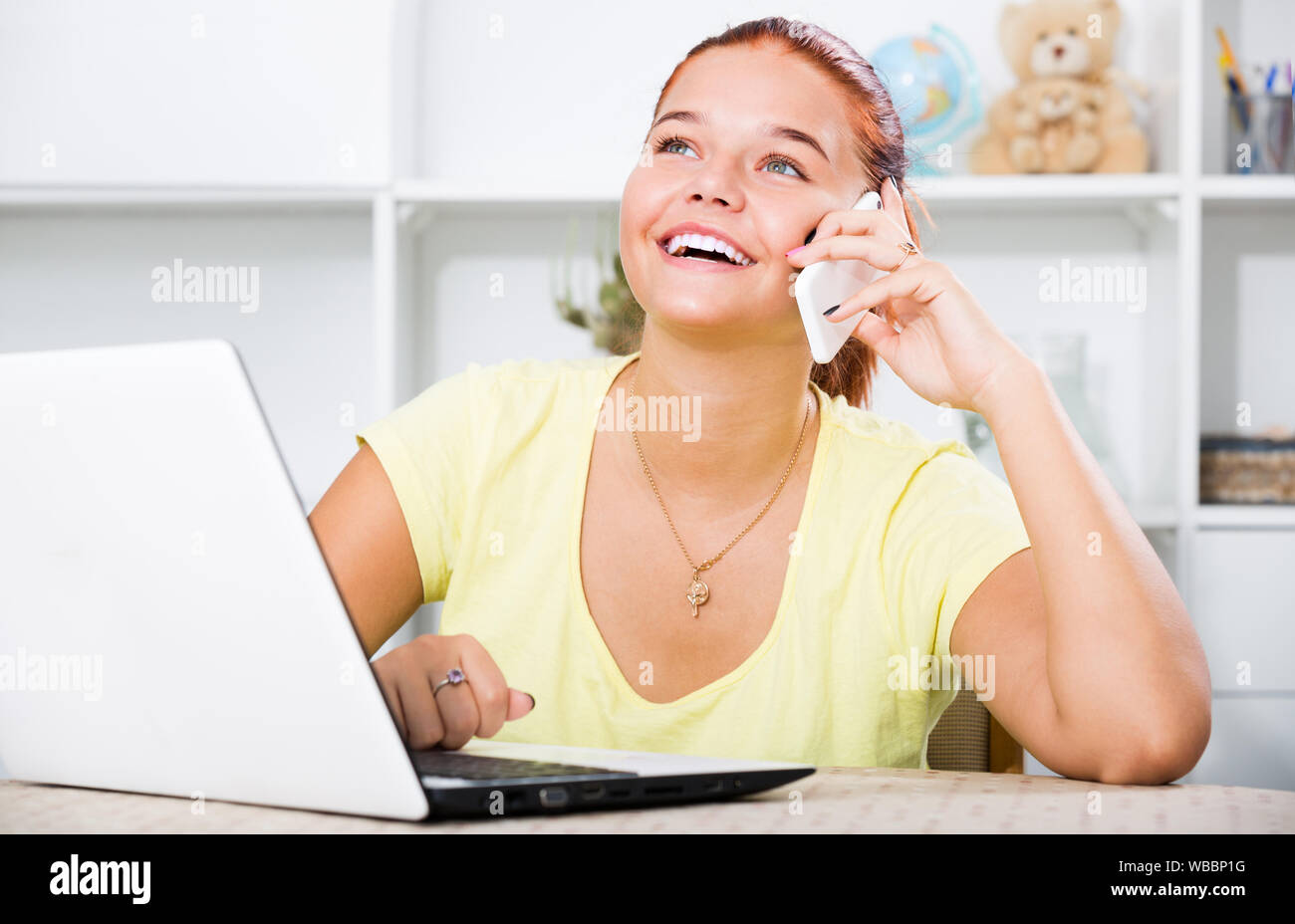 cheerful young female teenager student chatting on phone and typing on ...