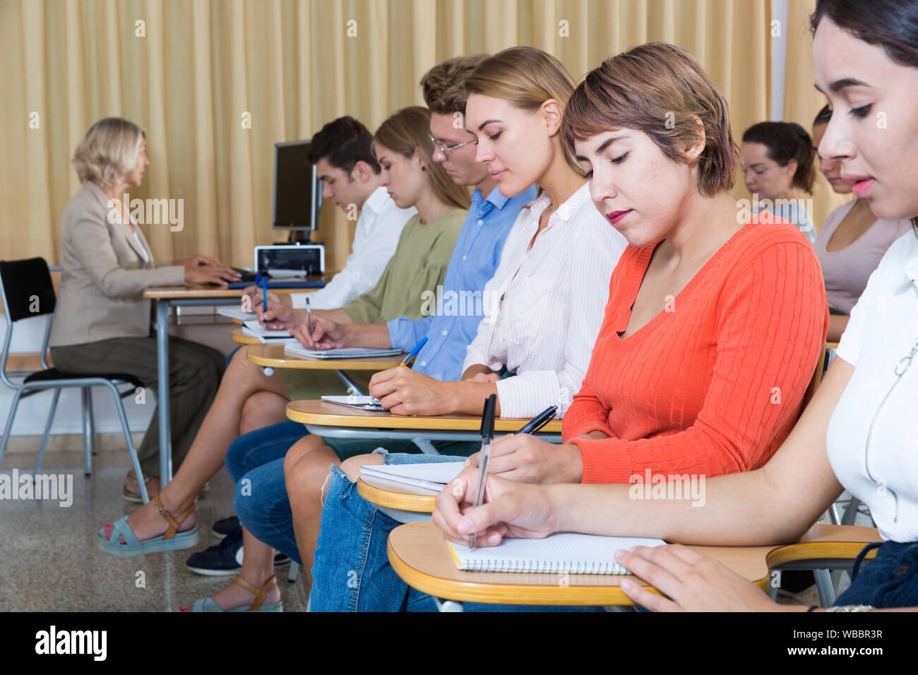 Side view of row of people listening female lecturer and making notes ...