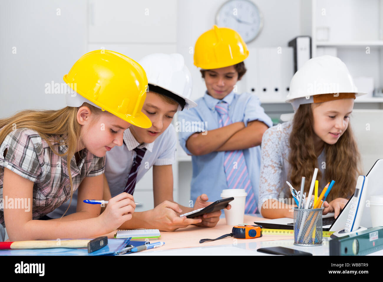 Teens in color helmet engineers discussing draft at the table Stock ...