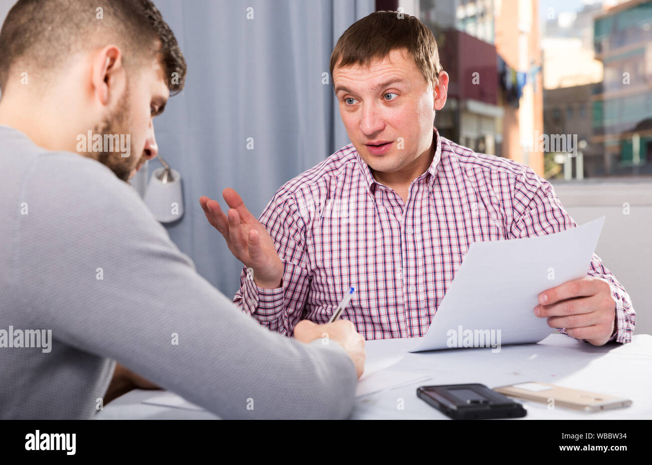Portrait of two men in serious discussion at home table while analysing ...