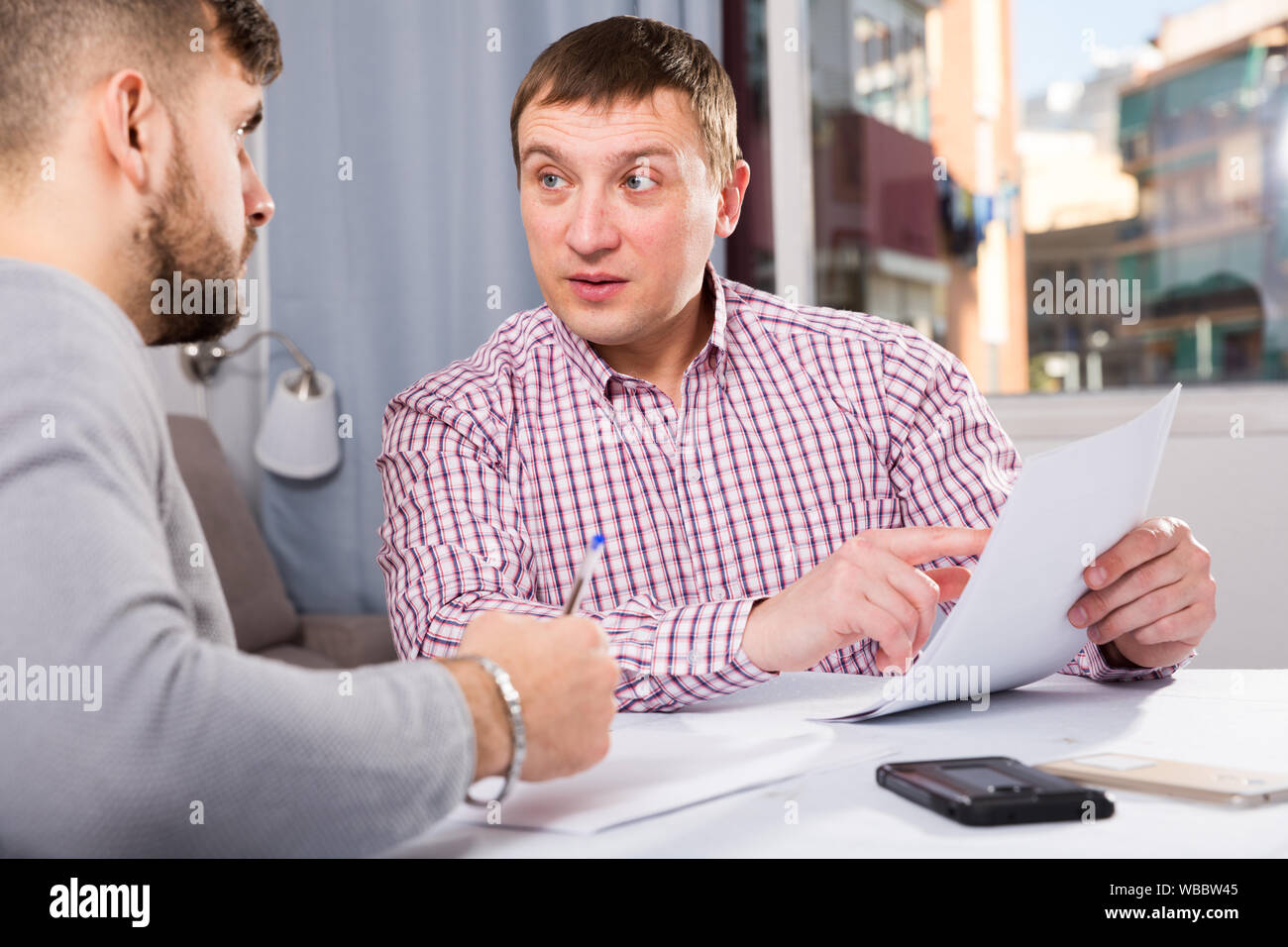 Portrait of two men in serious discussion at home table while analysing ...