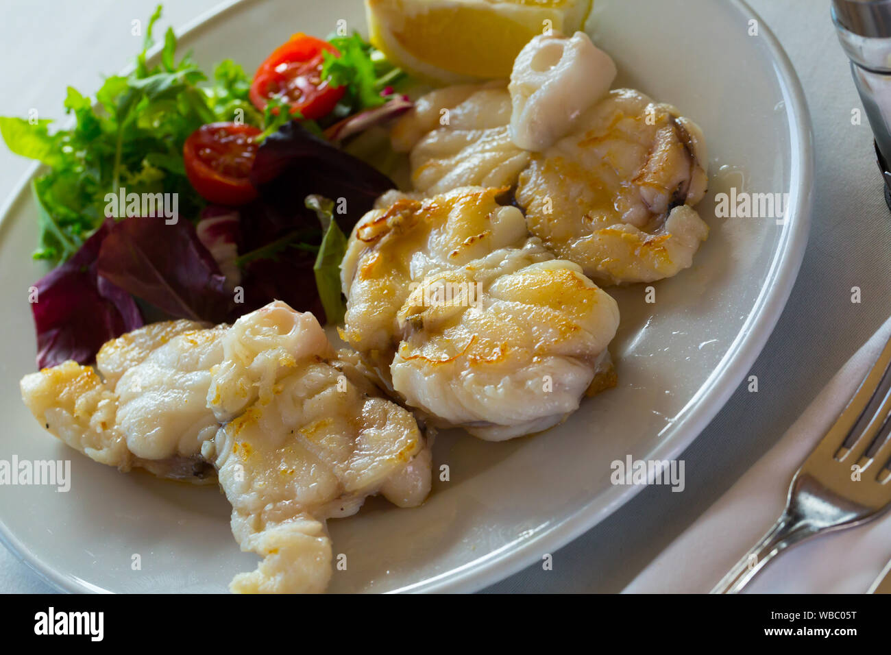 Baked angler fish served with lemon slice, salad leaves and cherry ...