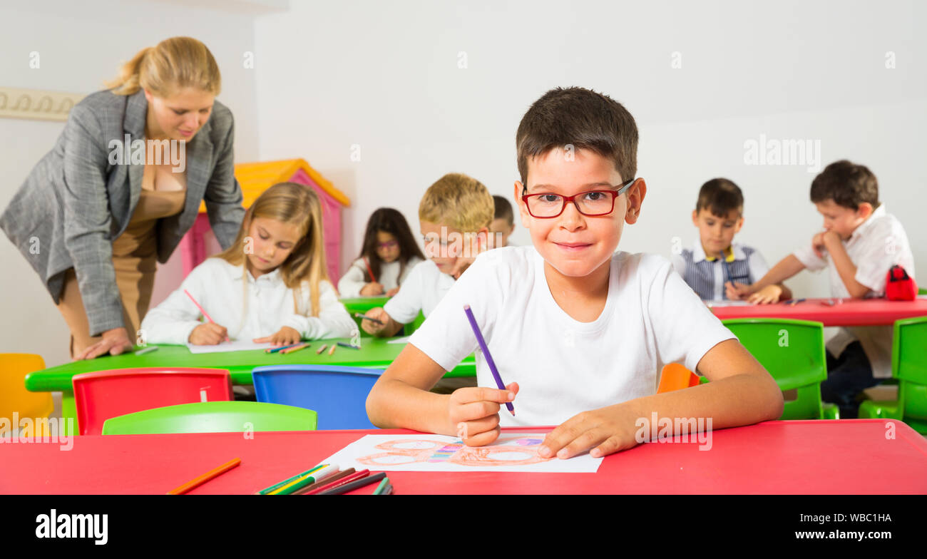 Portrait of boy student of primary school doing his task at desk in ...