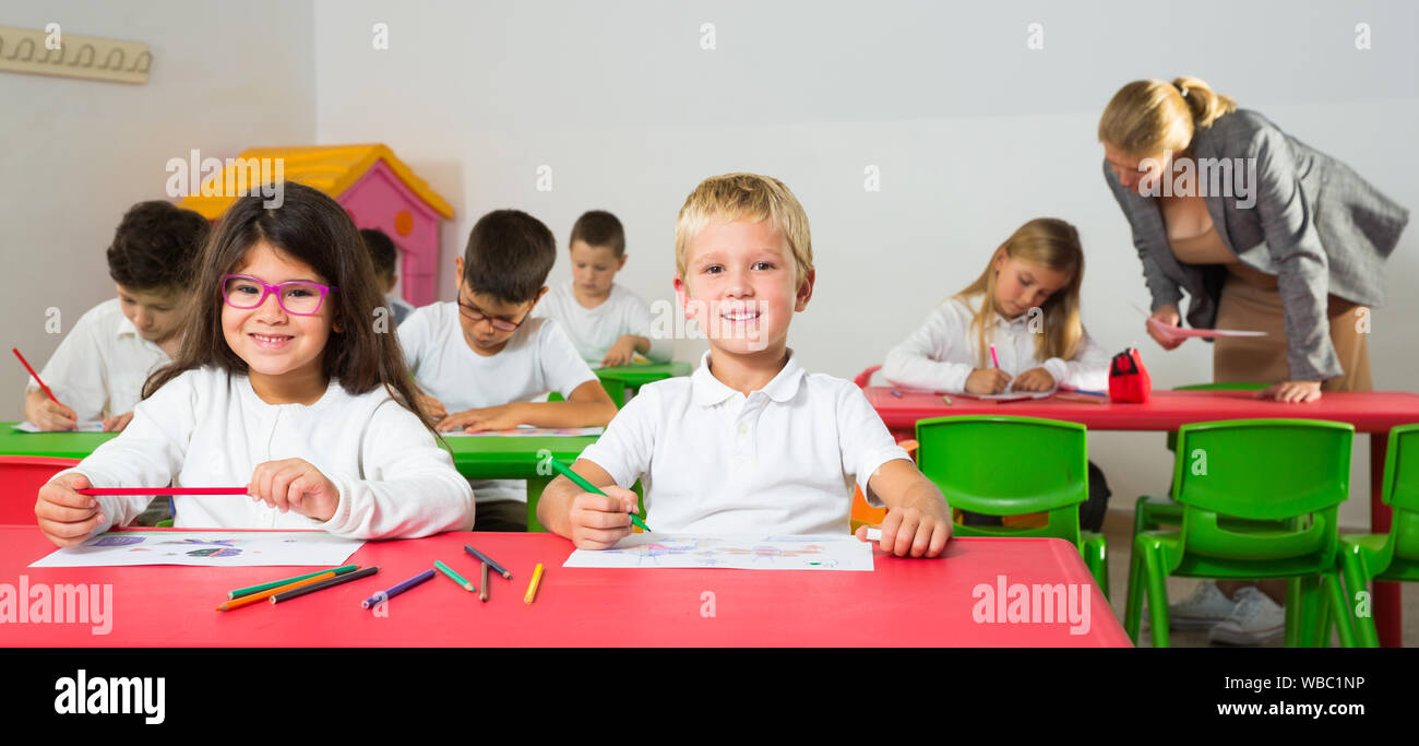 Portrait of two schoolkids and their teacher helping children in ...