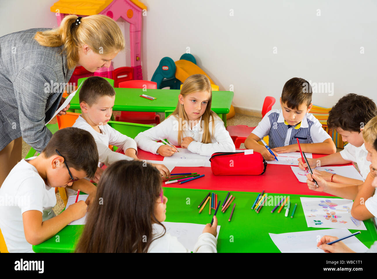 Happy female teacher helping schoolkids drawing with color pencils in ...