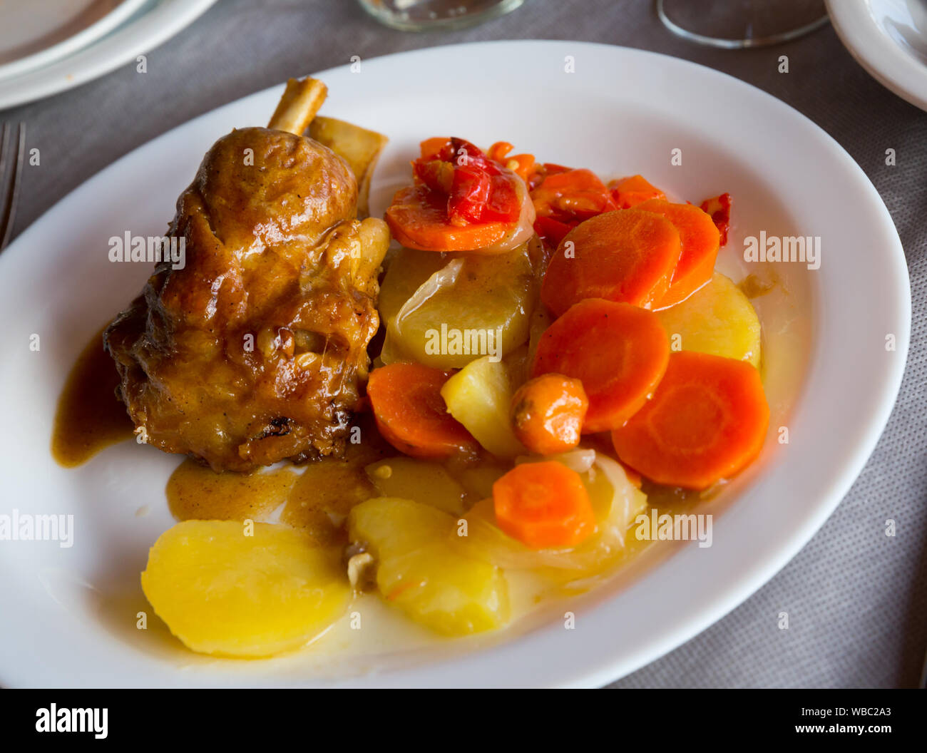 Appetizing baked pork knuckle (Codillo) with baked potatoes and carrot ...