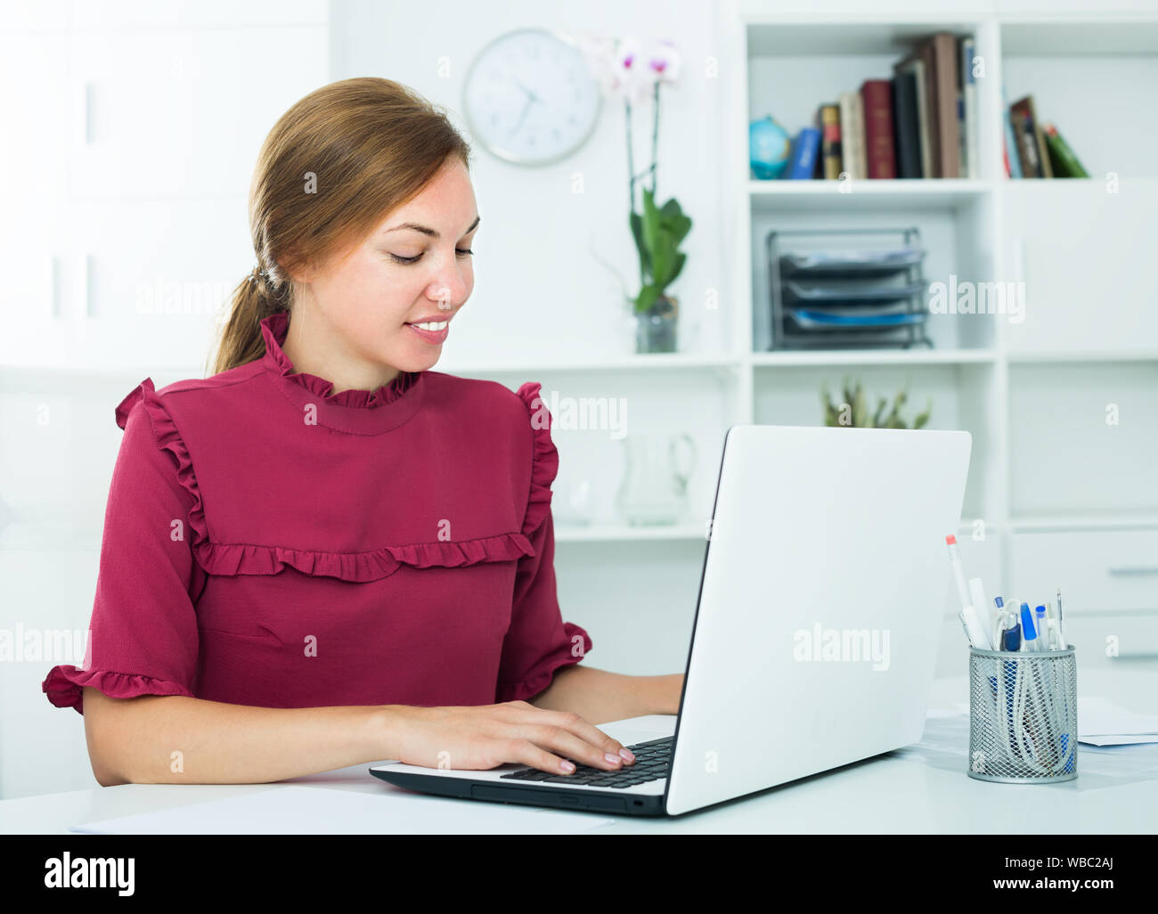 young charming female employee typing on portable computer at office ...