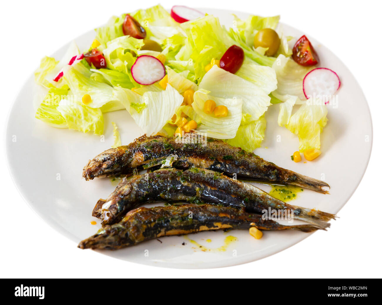 Roasted pilchards served on plate with fresh vegetable salad, corn and ...