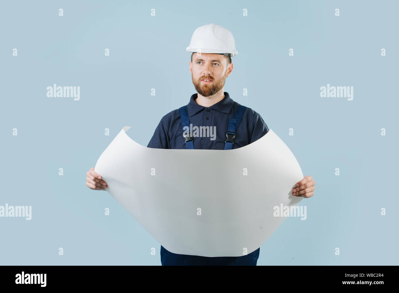 Construction engineer in a white helmet and blue uniform with a paper ...