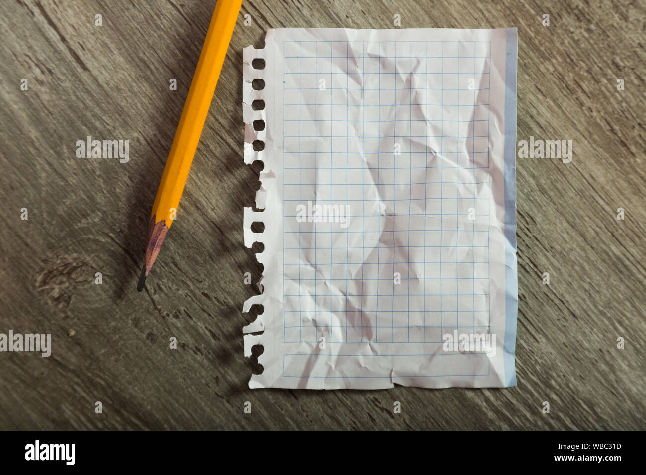 Crumpled notebook sheet in cage with pencil on table Stock Photo - Alamy