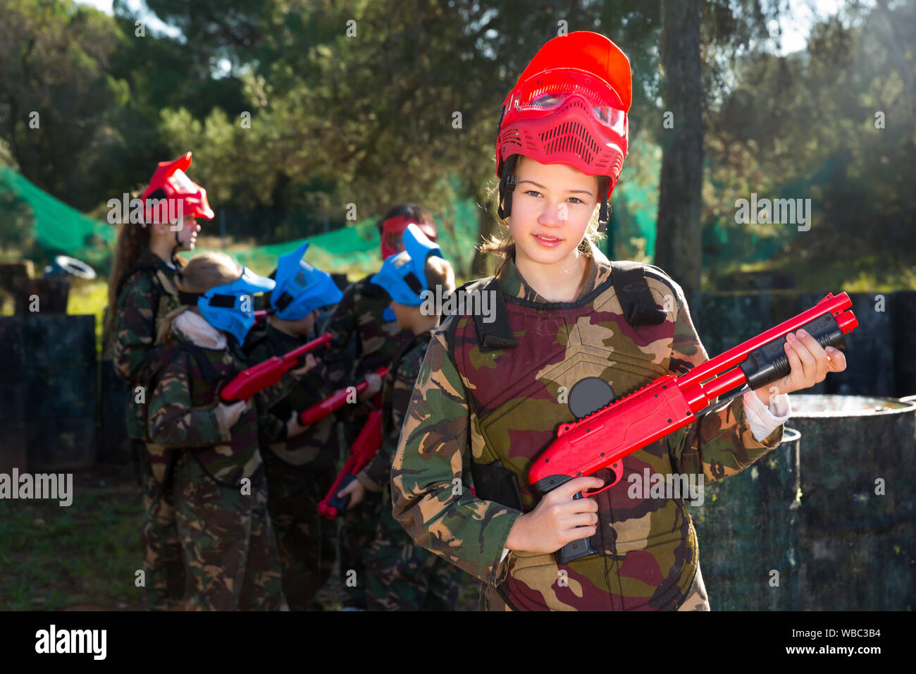 Portrait of cheerful tween girl paintball player with marker gun ready ...