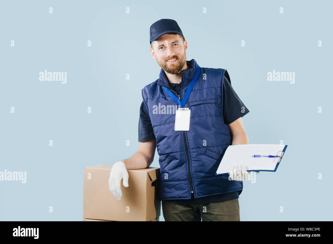 Delivery man in uniform holding signing form while leaning arm on a box ...