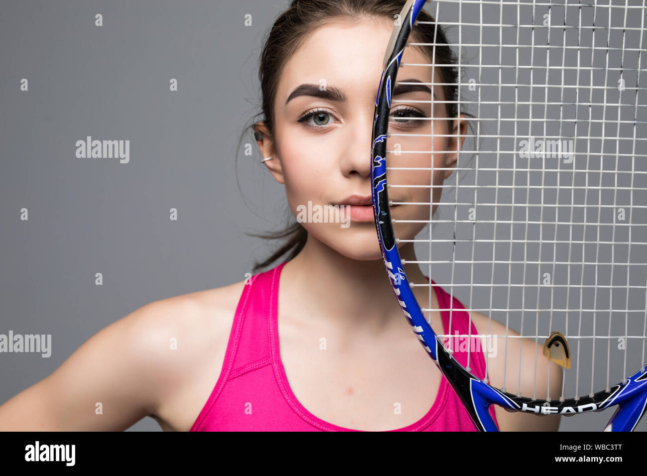 Woman with a tennis racket over her face. Neutral face and confident ...