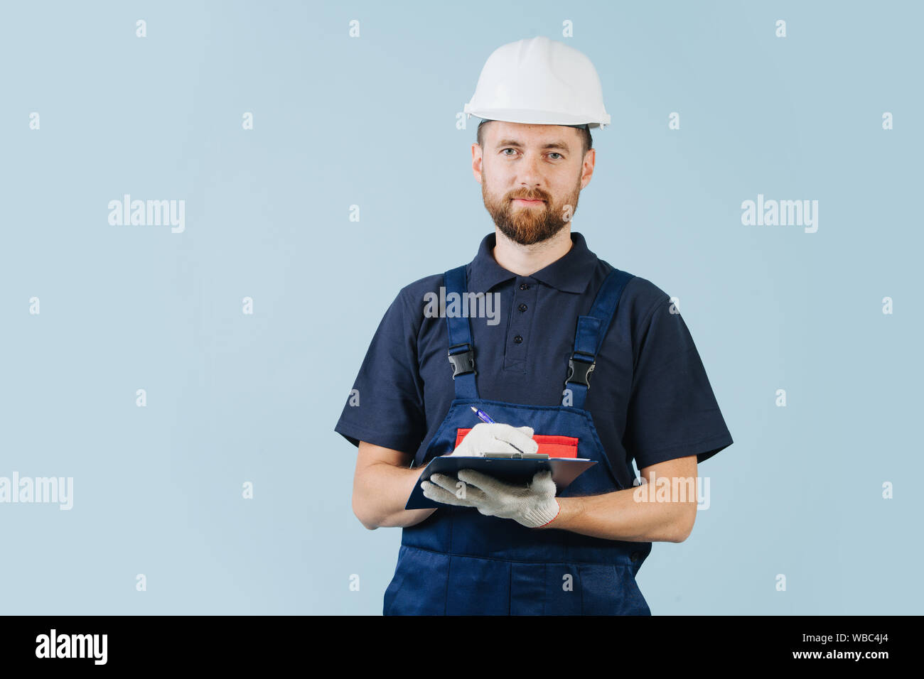 Construction engineer in a white helmet and blue uniform writing notes ...