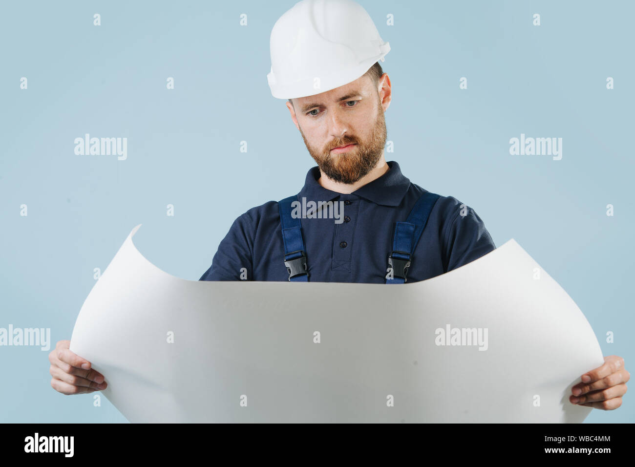 Construction engineer in a white helmet and blue uniform with a paper ...
