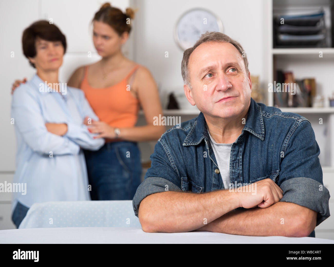Woman and her daughter are sympathying their sad father who is sitting ...