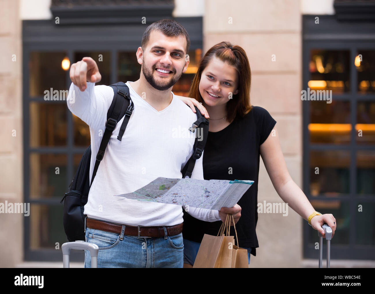 Couple of smiling tourists with map and baggage hugging at the street ...