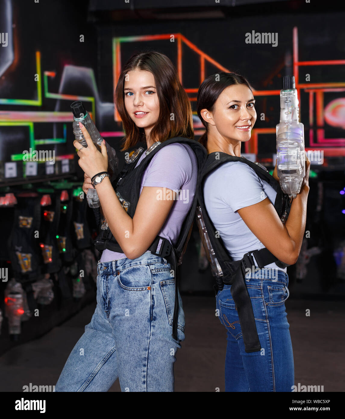 Two positive cheerful glad smiling girls standing back and holding guns ...