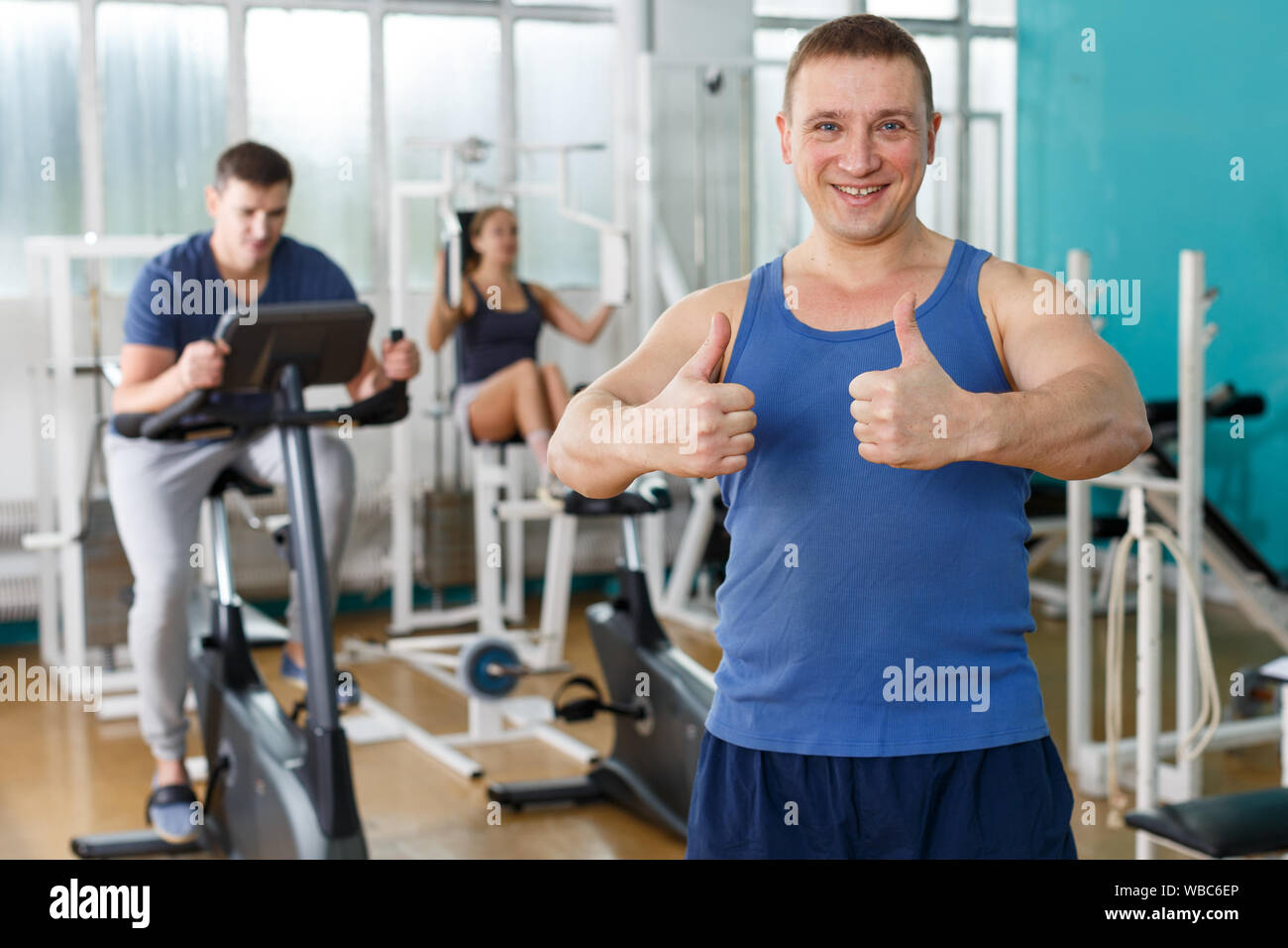 Muscular guy posing among sports equipment at gym Stock Photo - Alamy
