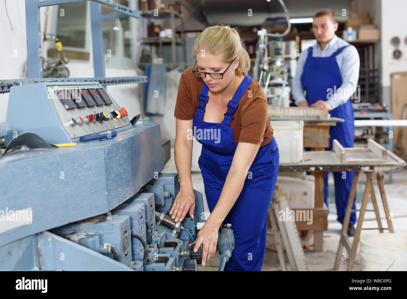 Glad female glazier working on glass straight line bevelling machine in ...