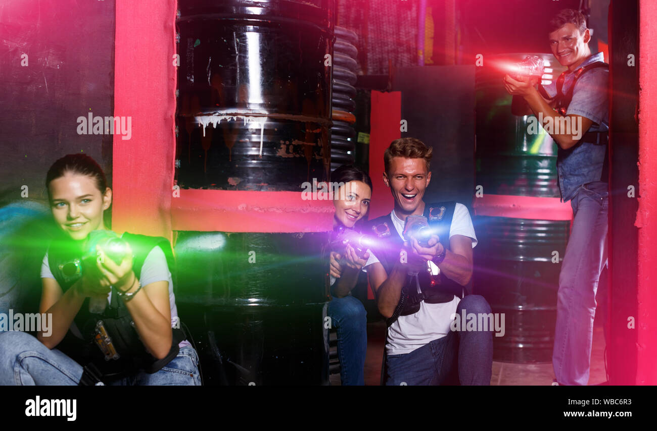 Group of smiling friends playing laser tag game with laser guns in ...