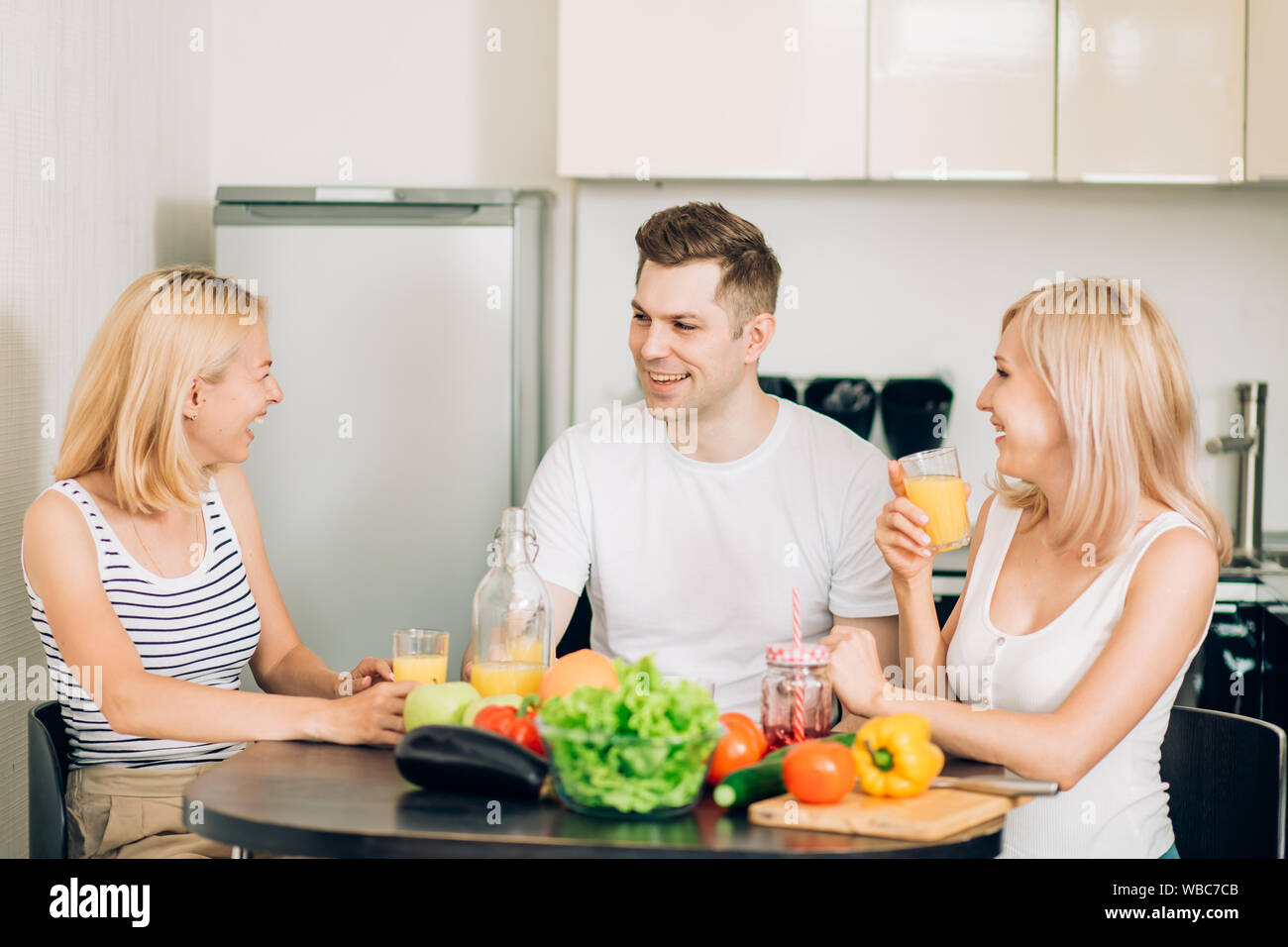 Students relaxing in kitchen. Three friends enjoying fresh juice ...